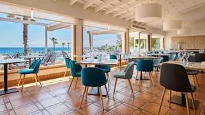 Restaurante com área externa e mesas voltadas para o mar, móveis modernos e grandes janelas.