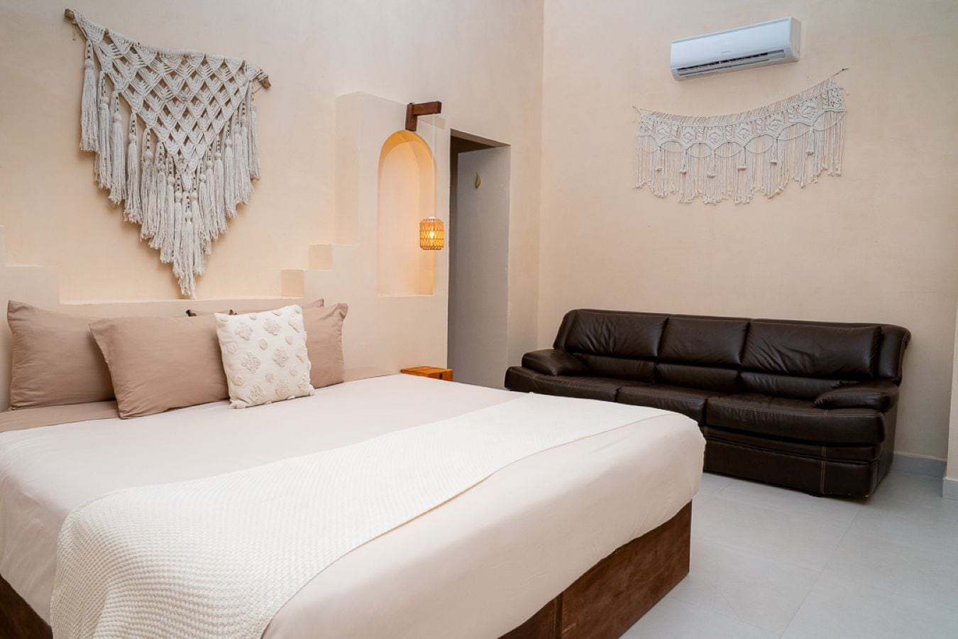 Quarto com cama, sofá de couro marrom e decoração nas paredes.