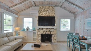 Uma sala de estar aconchegante com lareira de pedra, televisão de tela plana, sofá, mesa de centro e área de jantar com cadeiras.