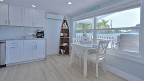 Uma cozinha moderna com armários brancos, um cantinho para café e uma área de refeições com vista para o mar.