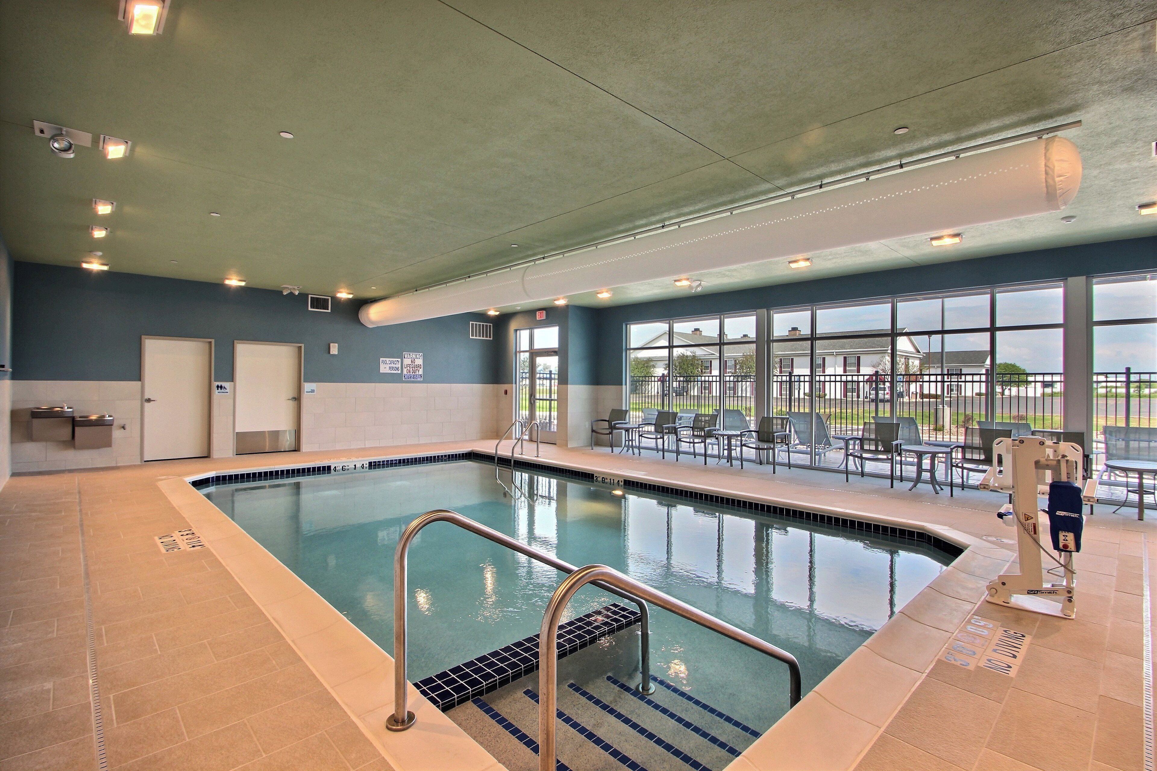 Piscina interna com água cristalina, cadeira de salva-vidas e vista para o exterior através de grandes janelas.