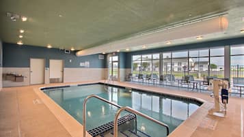 Piscina interna com água cristalina, cadeira de salva-vidas e vista para o exterior através de grandes janelas.