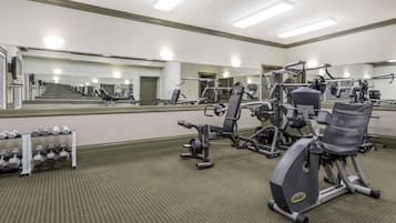 Uma academia com diversos equipamentos de exercícios, incluindo halteres, aparelho de supino e uma máquina elíptica.