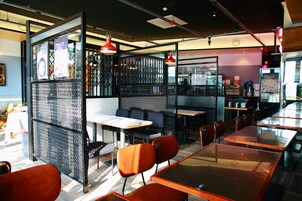 Um restaurante moderno com divisórias de vidro, mesas de madeira e cadeiras vermelhas.