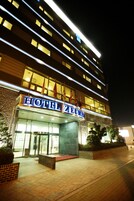 Entrada de hotel com uma placa indicando "HOTEL ZEUMEN" e bandeiras americanas.