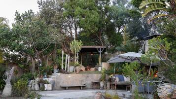 Uma área de piscina com espaço de estar coberto, degraus de pedra e diversas plantas.