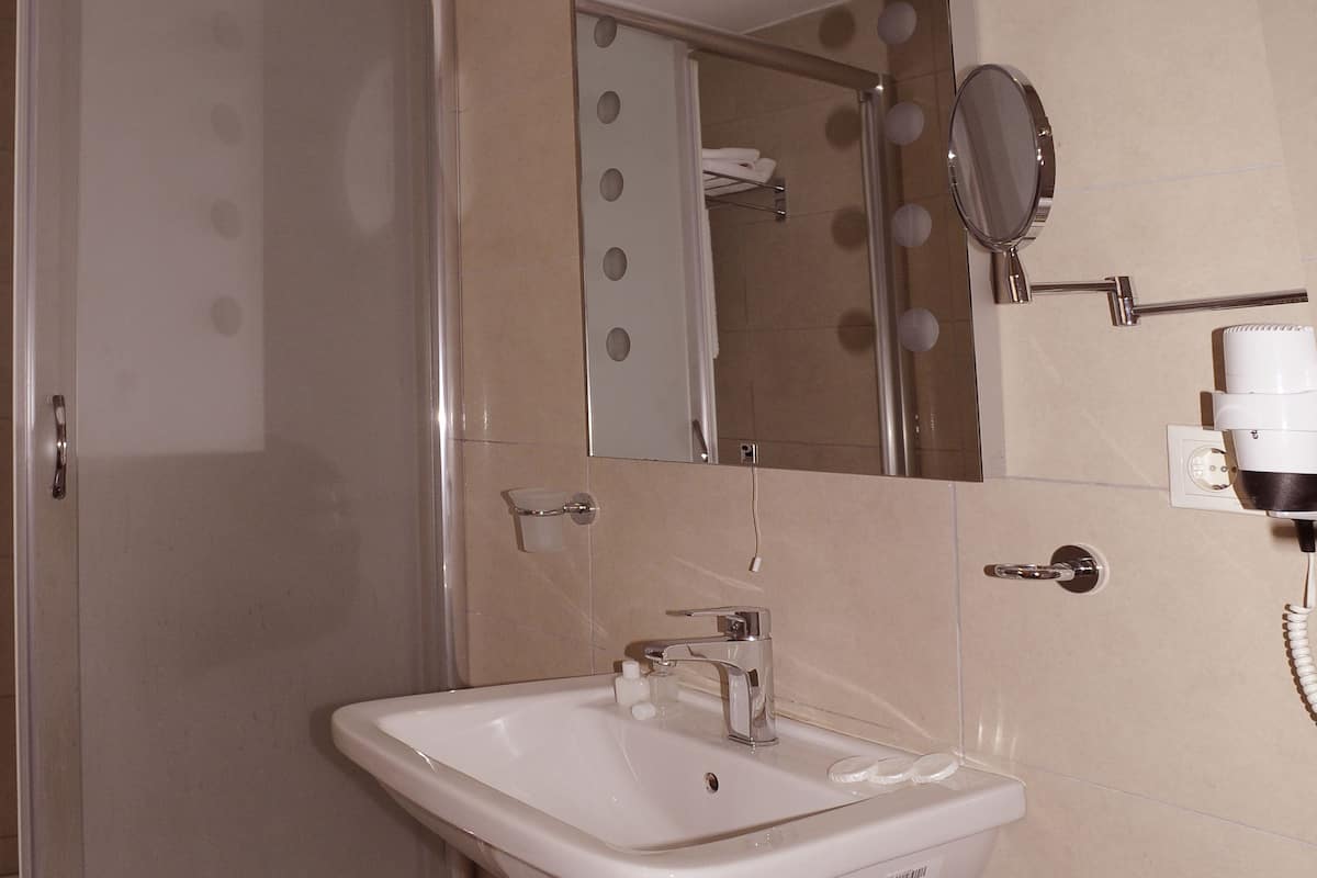 Casa de banho com chuveiro, lavatório, espelho e porta-toalhas.