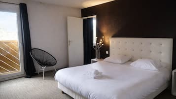 Quarto de hotel com uma cama grande, uma cadeira, uma mesa de cabeceira com abajur e vista através de uma porta de correr.
