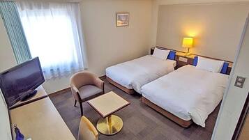 Quarto de hotel com duas camas, uma escrivaninha com televisão, uma cadeira e uma pequena mesa.