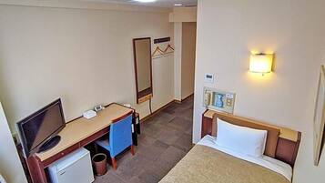 Quarto de hotel com uma cama, escrivaninha com computador, mini-geladeira, espelho e telefone fixado na parede.