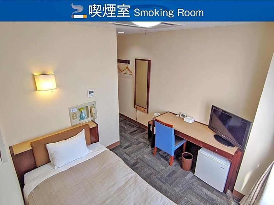 Quarto de hotel com cama, escrivaninha, televisão e pequeno frigorífico.