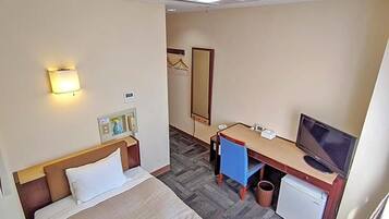 Quarto de hotel com cama, escrivaninha, televisão e pequeno frigorífico.