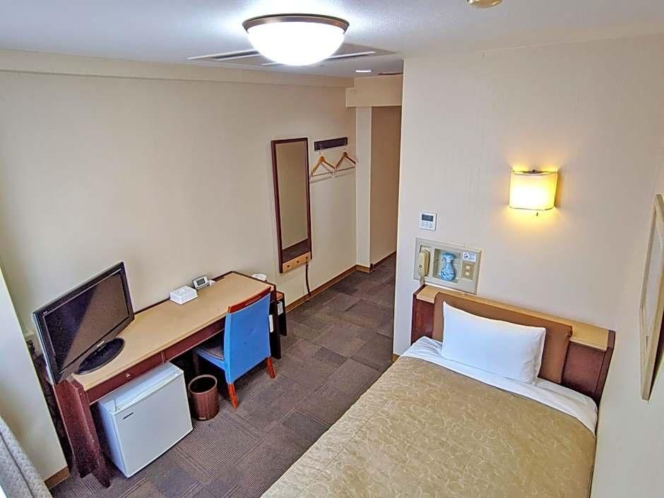 Quarto de hotel com cama, escrivaninha com computador, mini-geladeira, espelho e luminária de parede.