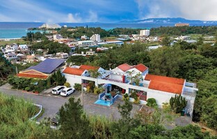 Um hotel à beira-mar com um edifício de telhado vermelho e uma piscina, oferecendo vista para o mar.
