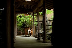 Um edifício japonês tradicional com estrutura de madeira, caminho de pedra e vegetação exuberante.