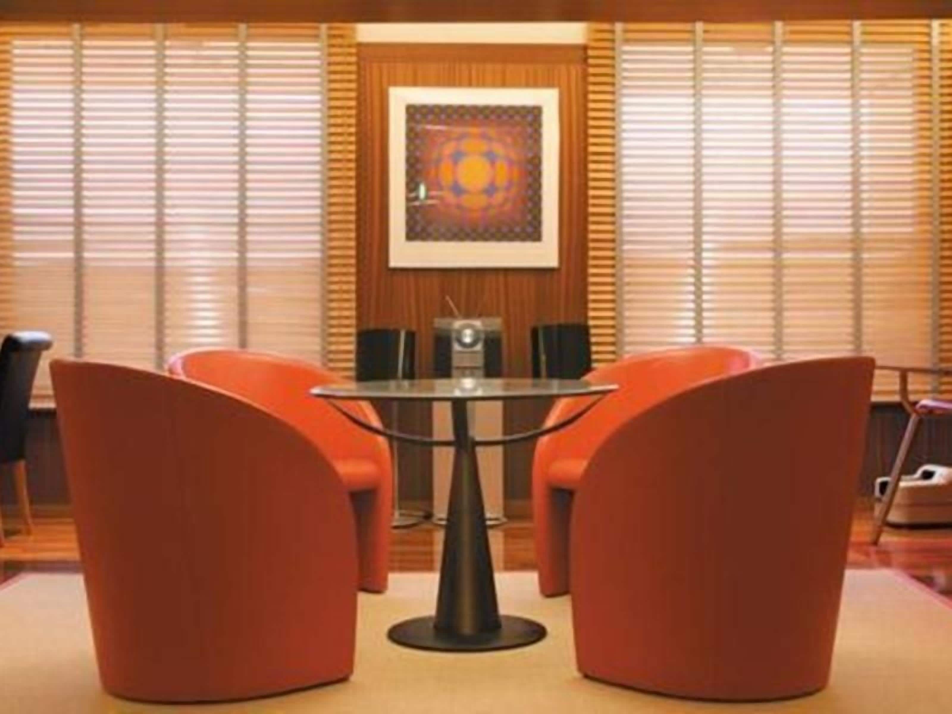 Um quarto com uma mesa redonda, quatro cadeiras laranja, uma obra de arte emoldurada na parede e venezianas de madeira.