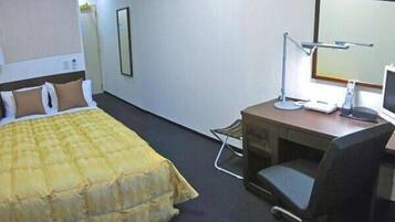 Quarto de hotel com cama, escrivaninha, cadeira, abajur, computador e espelho.
