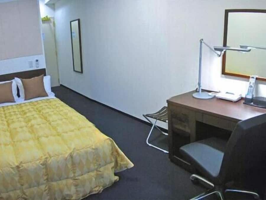 Quarto de hotel com cama, escrivaninha, cadeira, abajur, computador e espelho.
