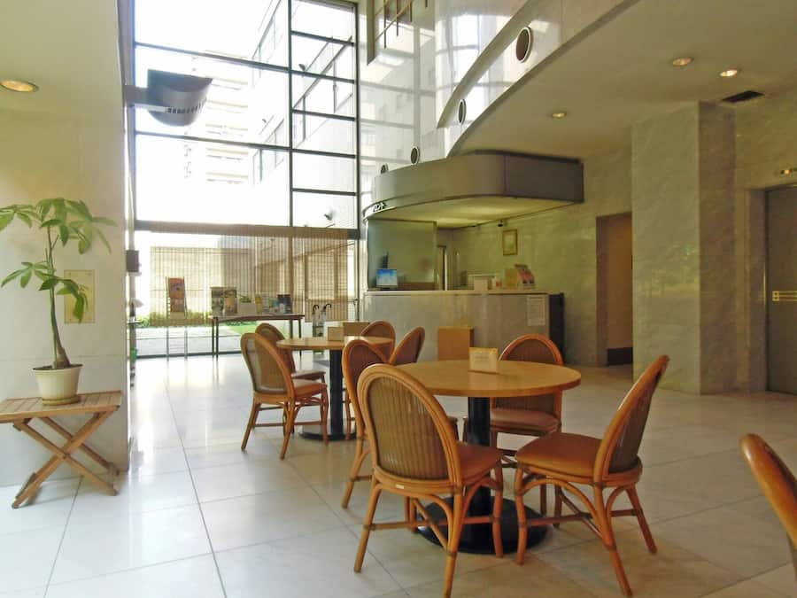 Uma sala de jantar moderna com uma mesa redonda e cadeiras de vime, janelas amplas e um vaso com planta.