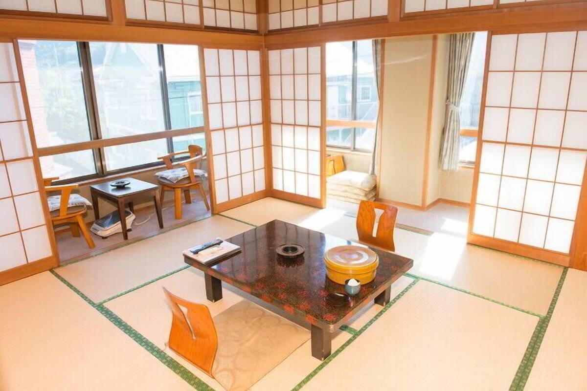 Um quarto japonês tradicional com tatames, uma mesa baixa com almofada e portas shoji deslizantes.
