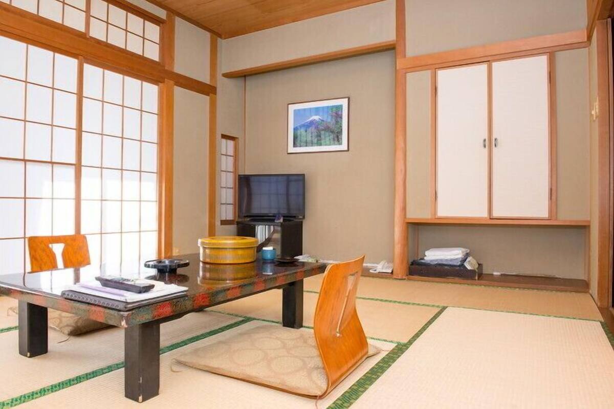 Um quarto japonês tradicional com tatames, uma mesa baixa com almofadas, uma televisão e um armário com portas de correr.