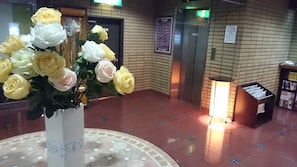Um hall com piso de azulejos, um pilar branco com design floral e um vaso com rosas amarelas e brancas.