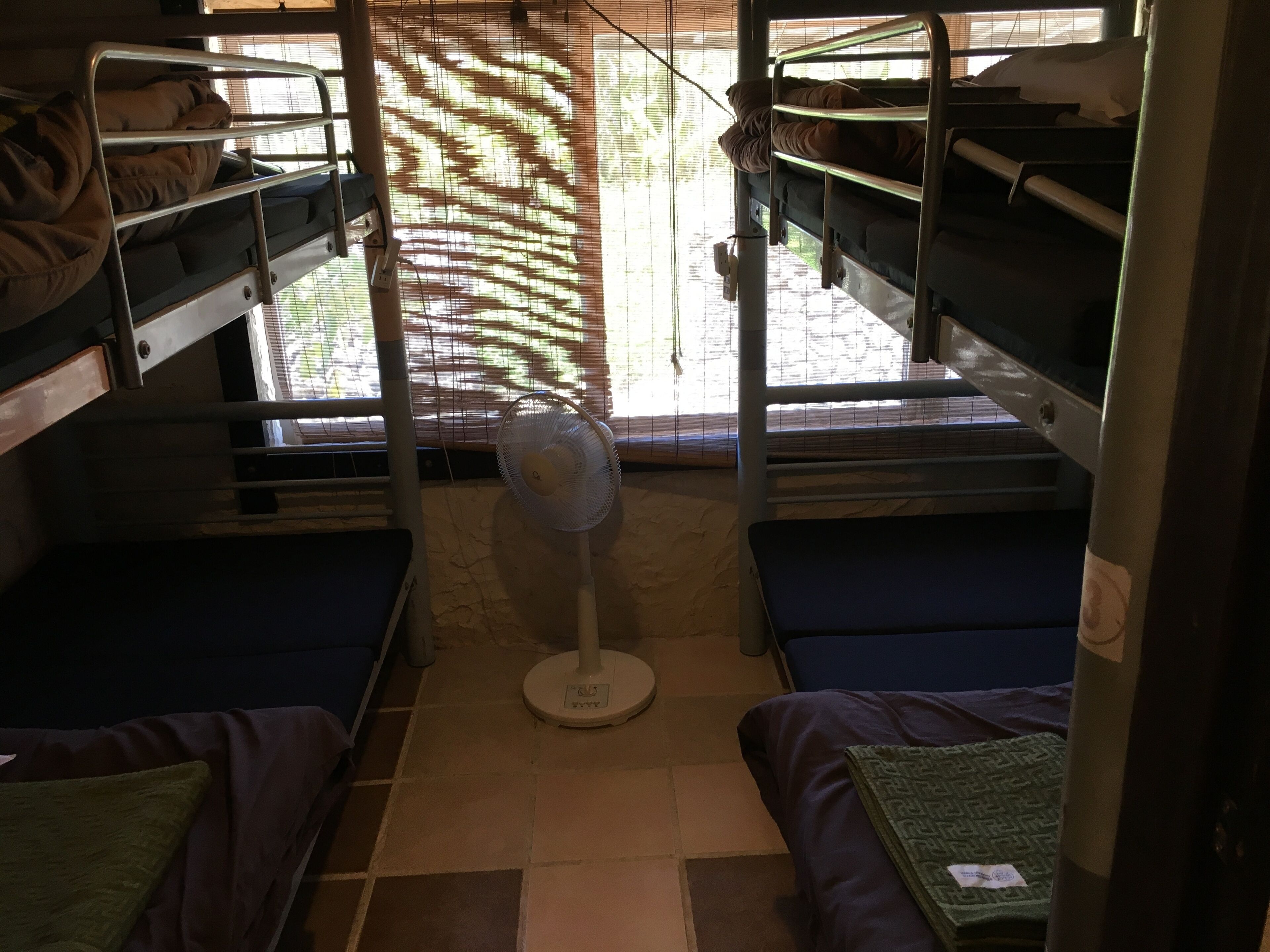 Um quarto em dormitório com beliches, um ventilador e uma janela com persianas.