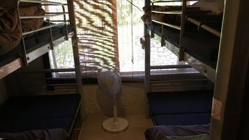 Um quarto em dormitório com beliches, um ventilador e uma janela com persianas.