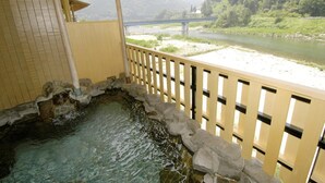 Uma área de águas termais com um deque de madeira que dá para um rio e uma ponte ao fundo.