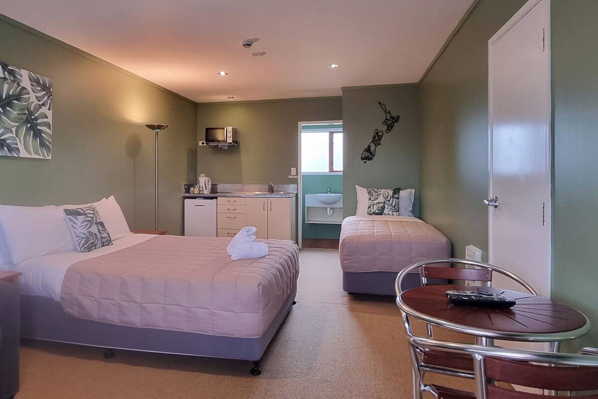 Quarto de hotel com duas camas, uma kitchenette pequena, banheiro e área de refeições.