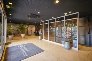 Um hall moderno com balcão de recepção, plantas em vasos e divisória de vidro com padrões decorativos.