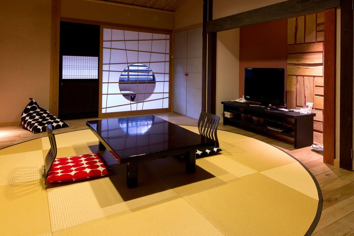 Um quarto japonês tradicional com tatames, uma mesa baixa, uma televisão e uma porta deslizante.