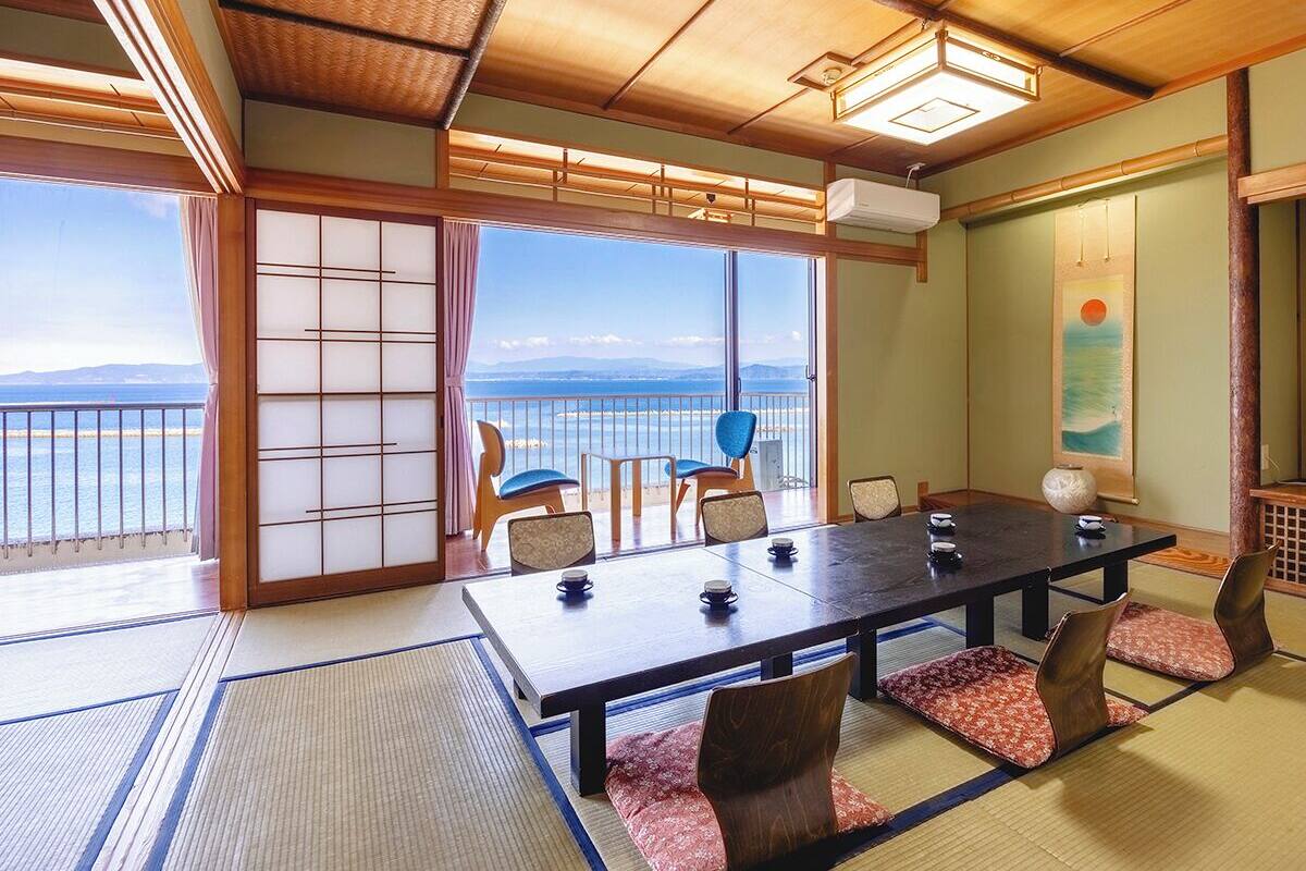 Um quarto japonês tradicional com tatames, uma mesa baixa com almofadas e vista para o mar.