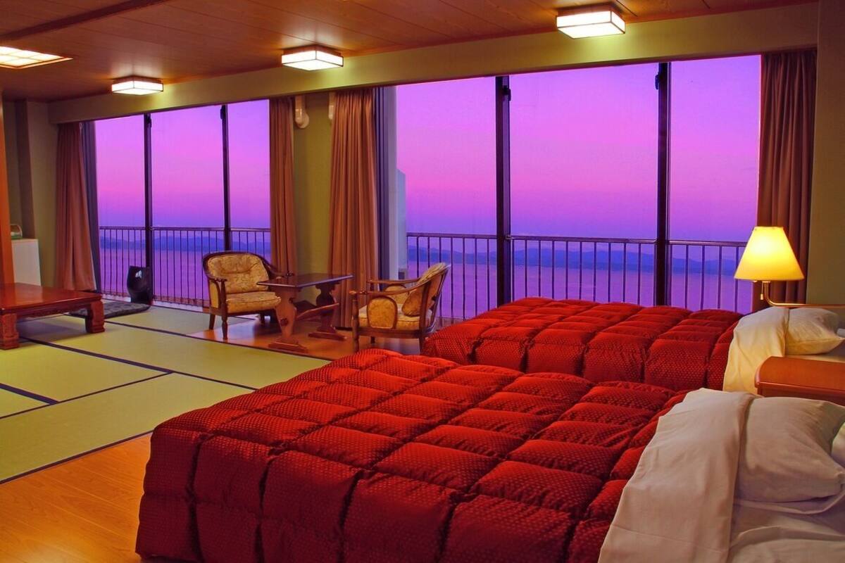 Quarto de hotel com duas camas, uma cadeira, uma mesa e vista para o mar.