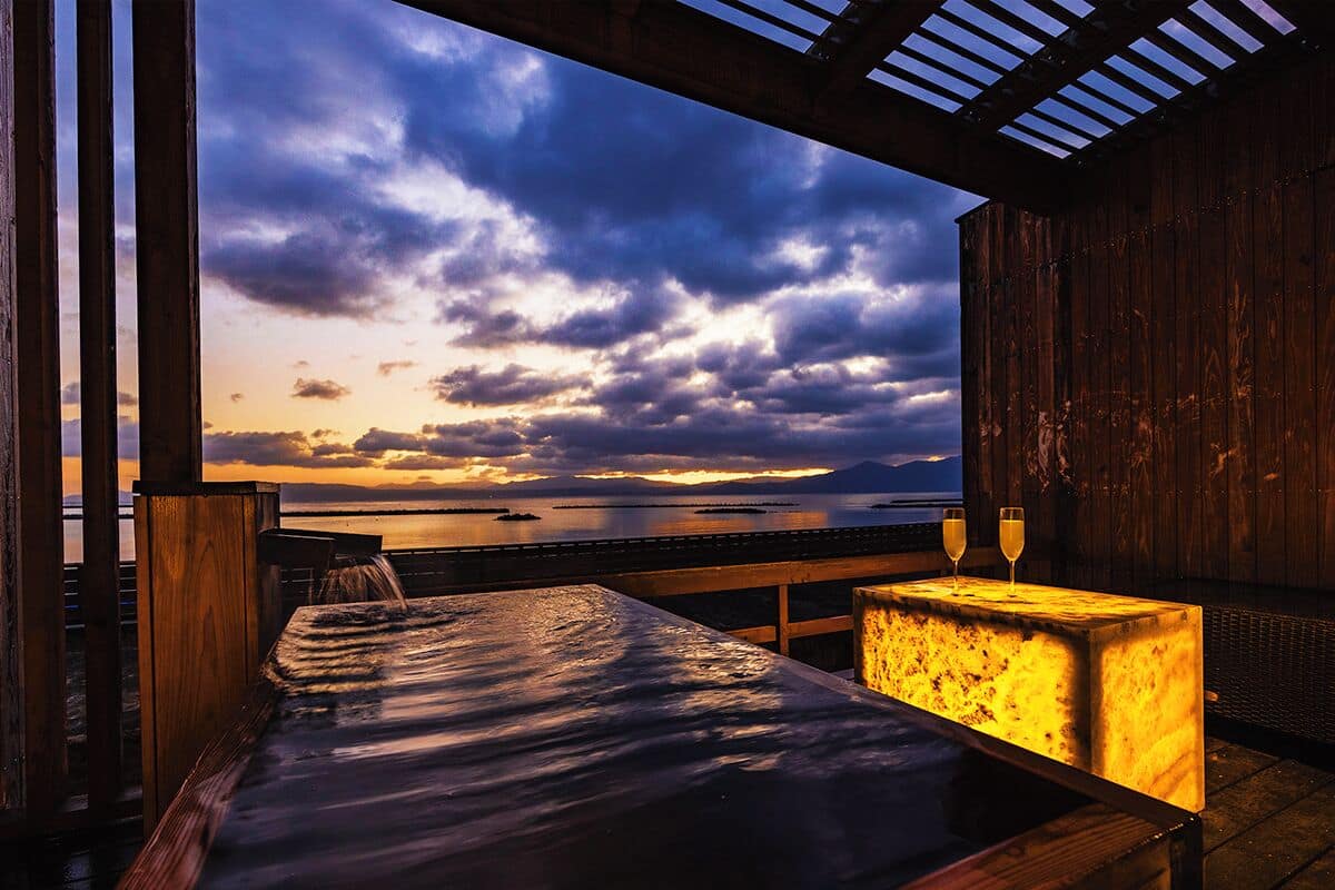 Uma banheira de hidromassagem com deck de madeira e vista para o oceano e o pôr do sol.