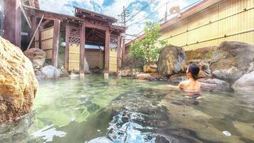 Uma onsen japonesa tradicional com água cristalina, estruturas de madeira e pedras grandes.