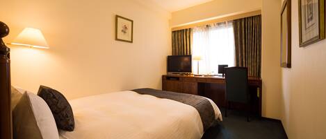 Quarto de hotel com cama, escrivaninha, cadeira, televisão e janela com cortinas.