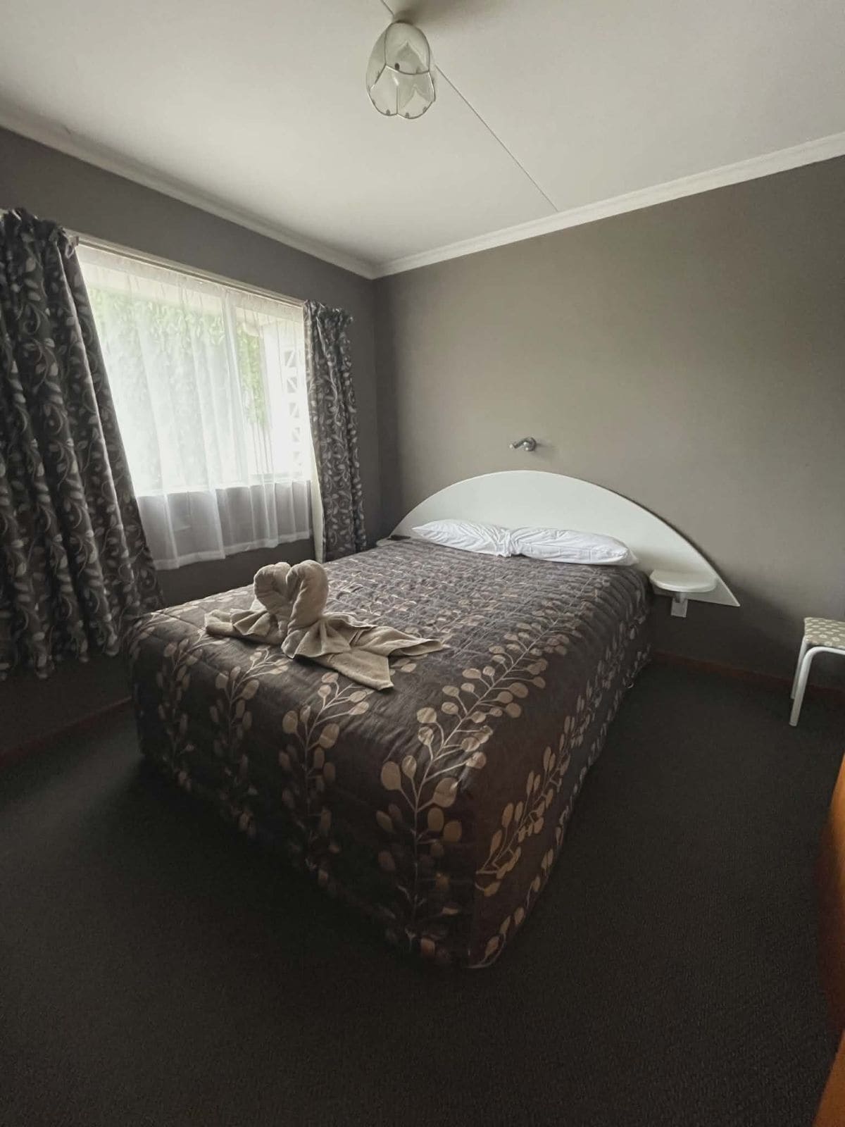 Quarto com cama, mesa de cabeceira, janela com cortinas e luminária no teto.