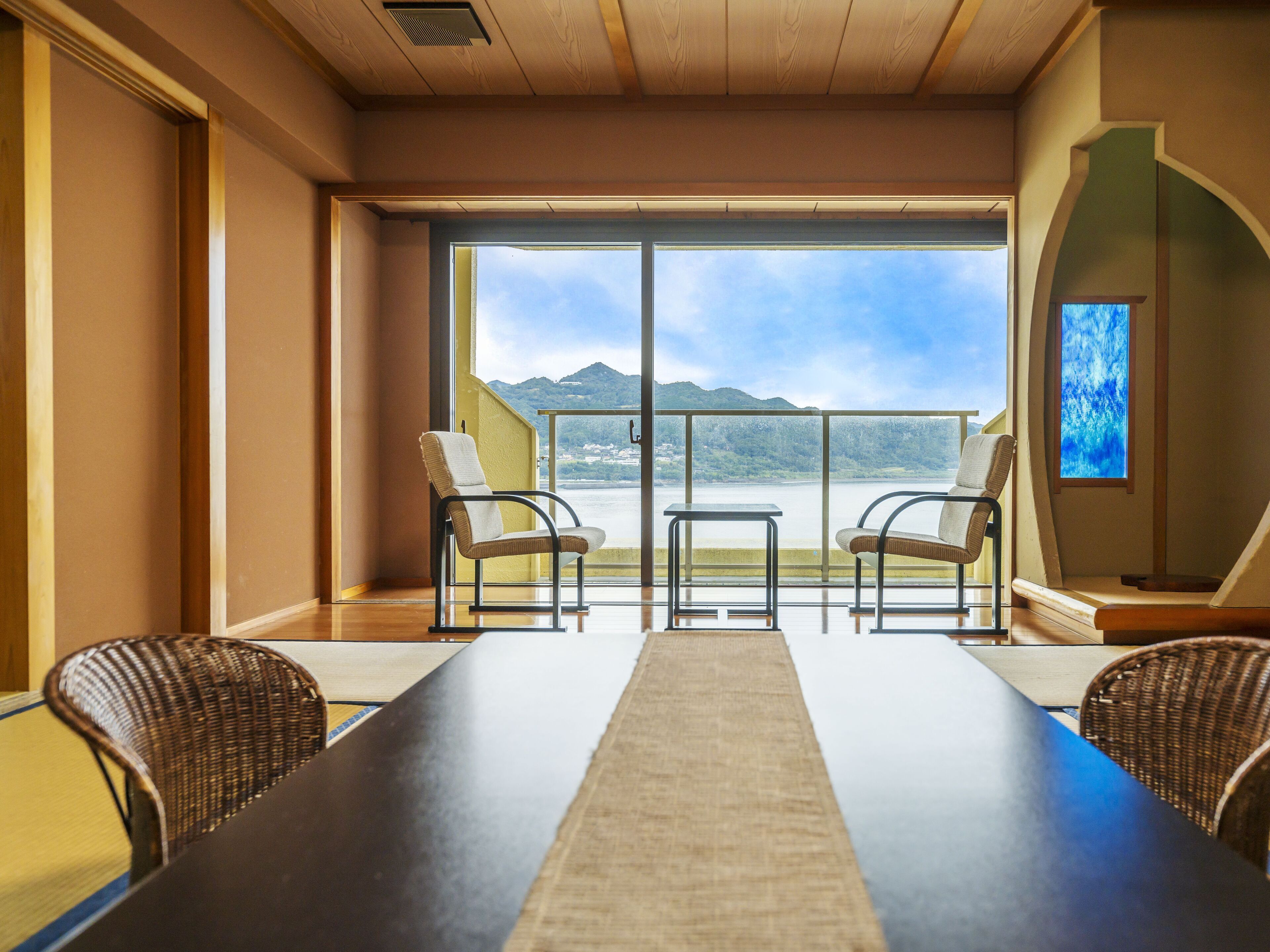 Uma sala de conferência com uma mesa grande e duas cadeiras, vista para um lago e montanhas através de grandes portas de vidro, e um design de interiores moderno.