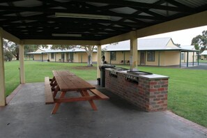 Uma área de piquenique coberta com uma mesa de madeira e um espaço para churrasco.