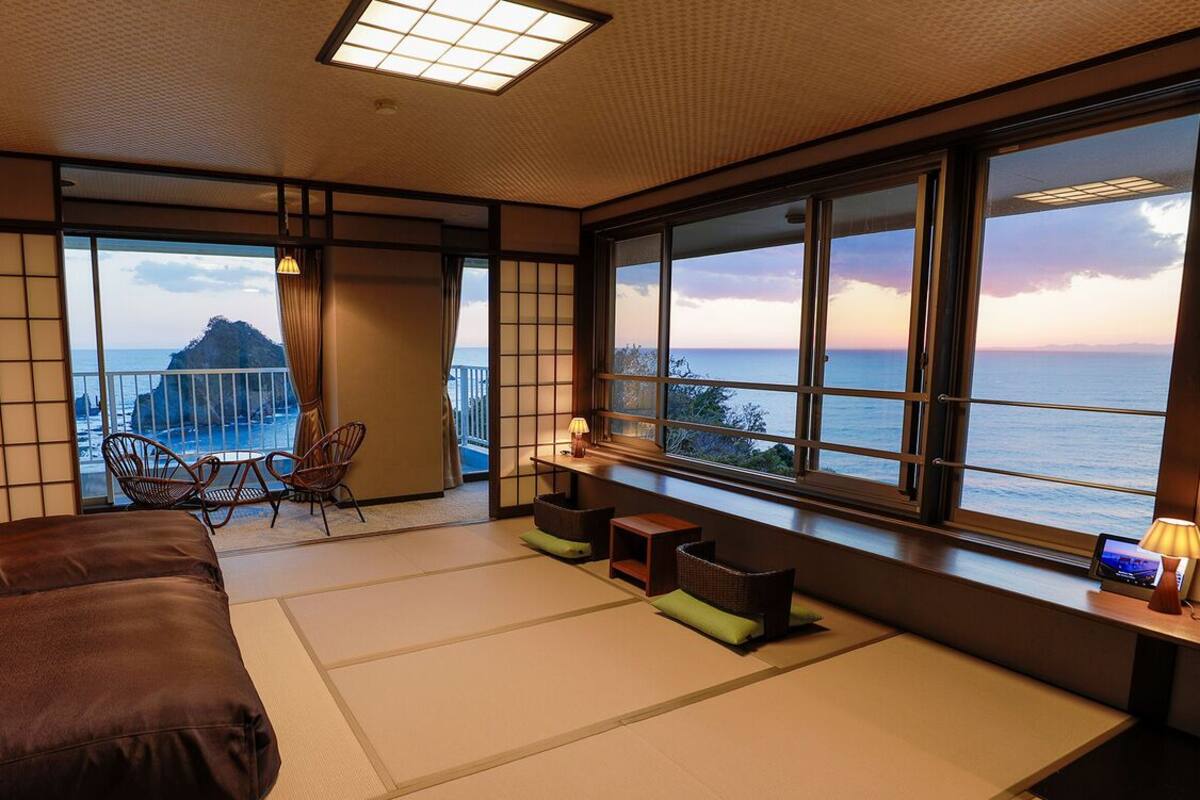 Quarto com piso de tatame, cama, área de estar com almofadas e vista para o mar.