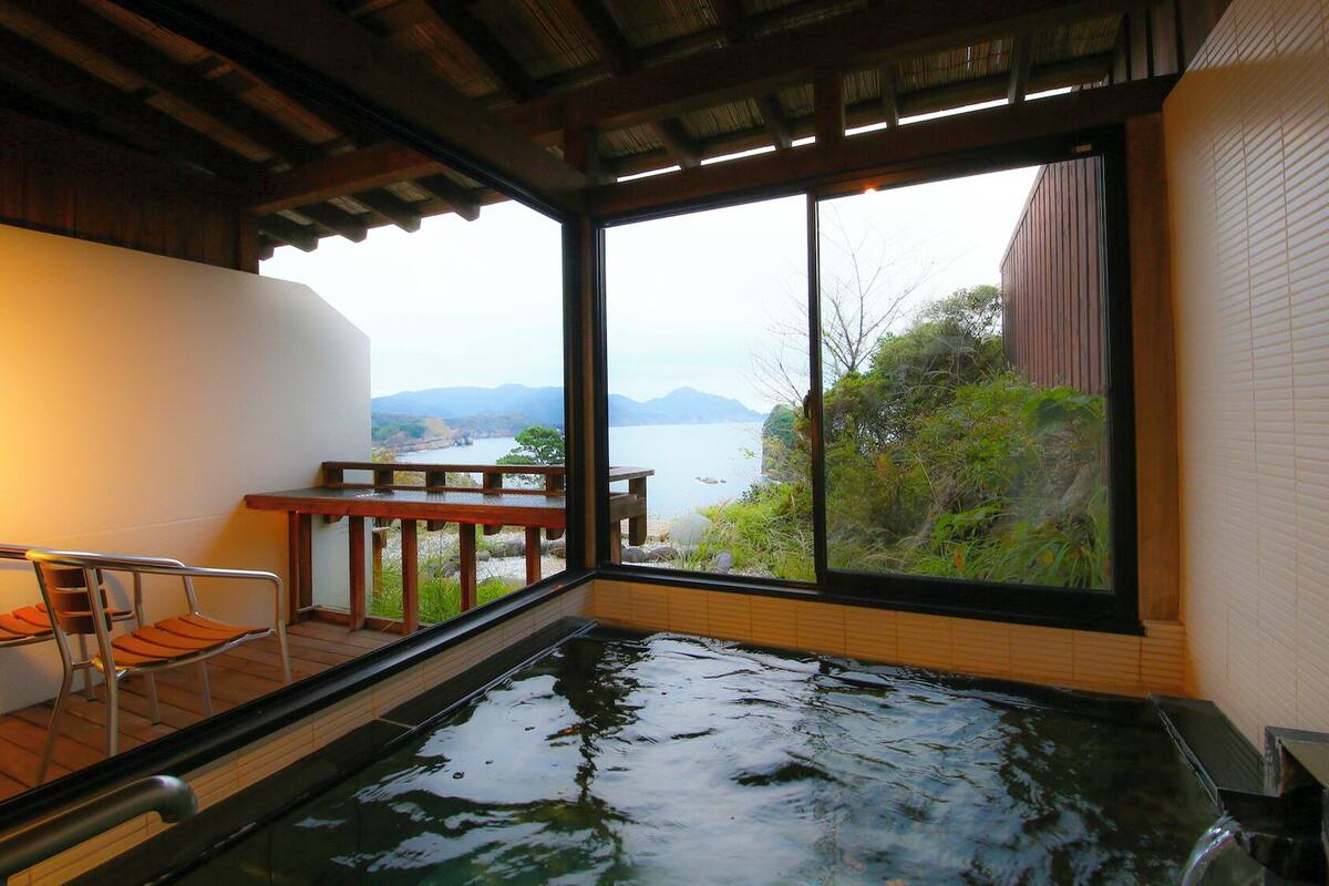 Uma banheira de hidromassagem com vista para um lago e montanhas, uma mesa de madeira e uma cadeira.