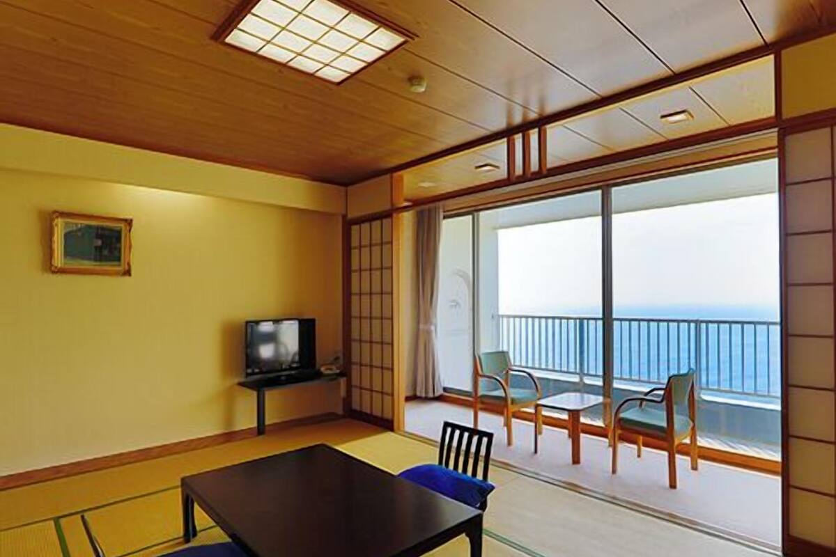 Quarto com piso de tatame, mesa baixa, televisão e varanda com vista.