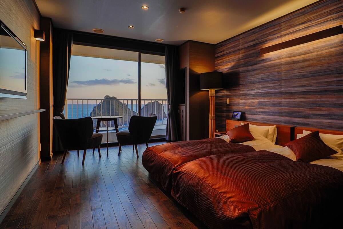 Quarto de hotel moderno com uma cama grande, uma varanda e vista, e uma parede de madeira.
