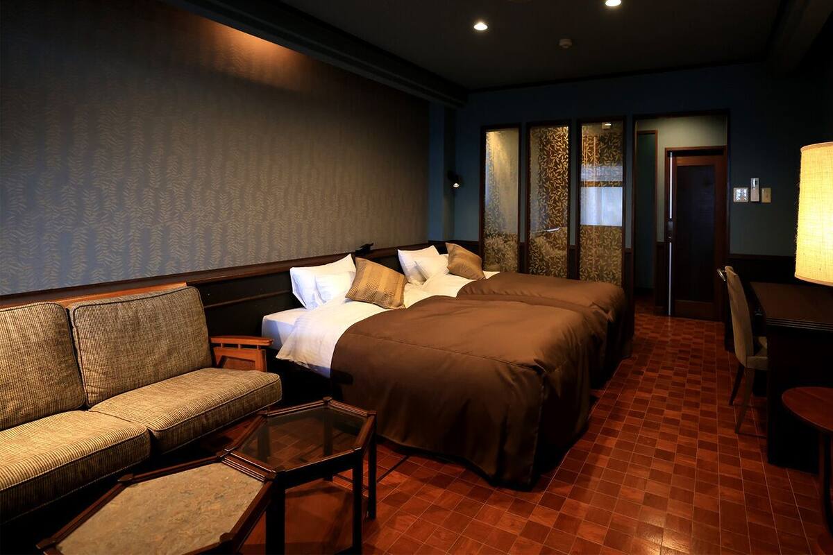 Quarto de hotel com sofá, duas camas, escrivaninha e abajur.