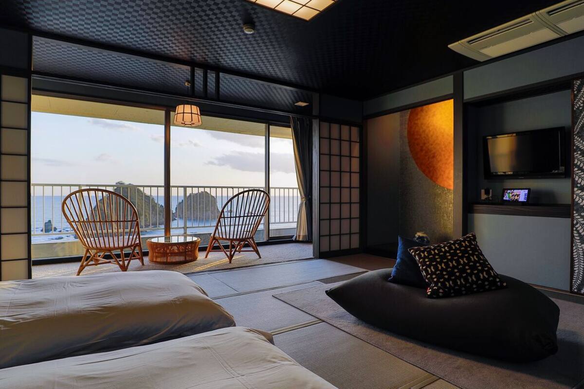 Quarto de hotel moderno com uma janela grande, uma cama, área de estar e uma televisão.