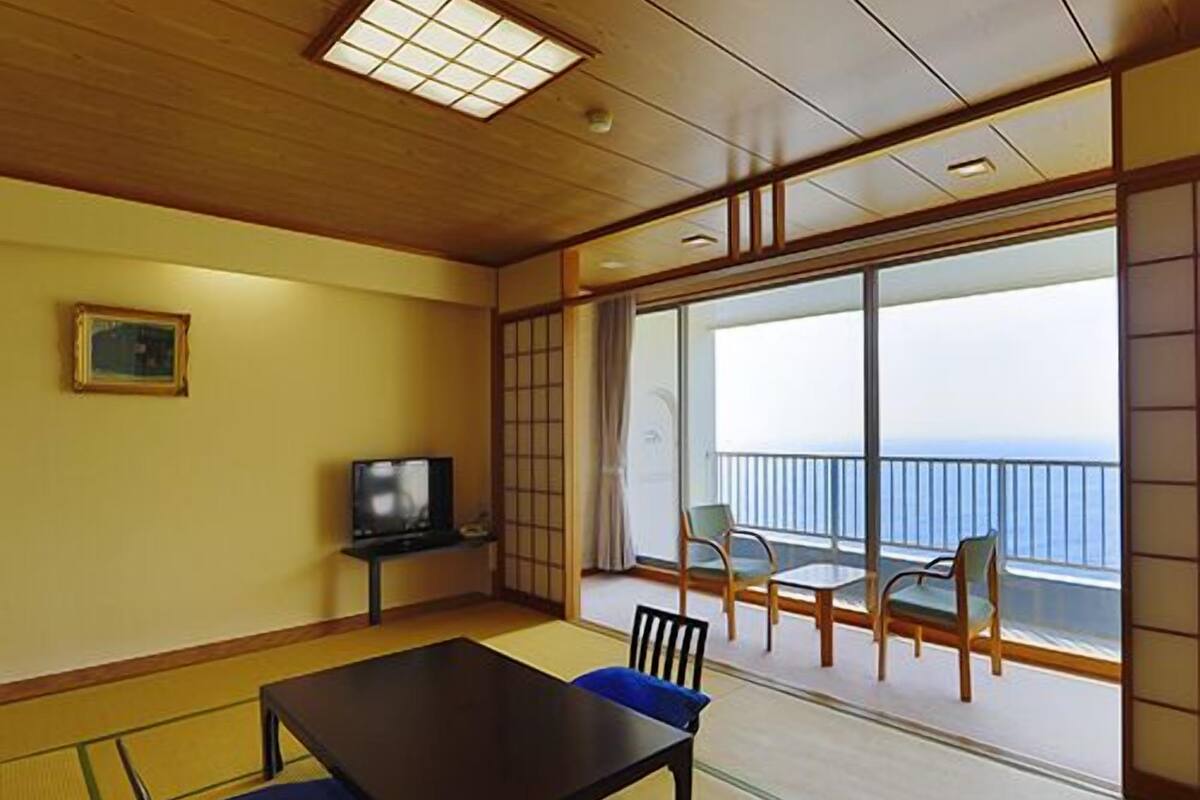 Quarto com tatames, mesa baixa, cadeiras, televisão e uma grande janela com vista.