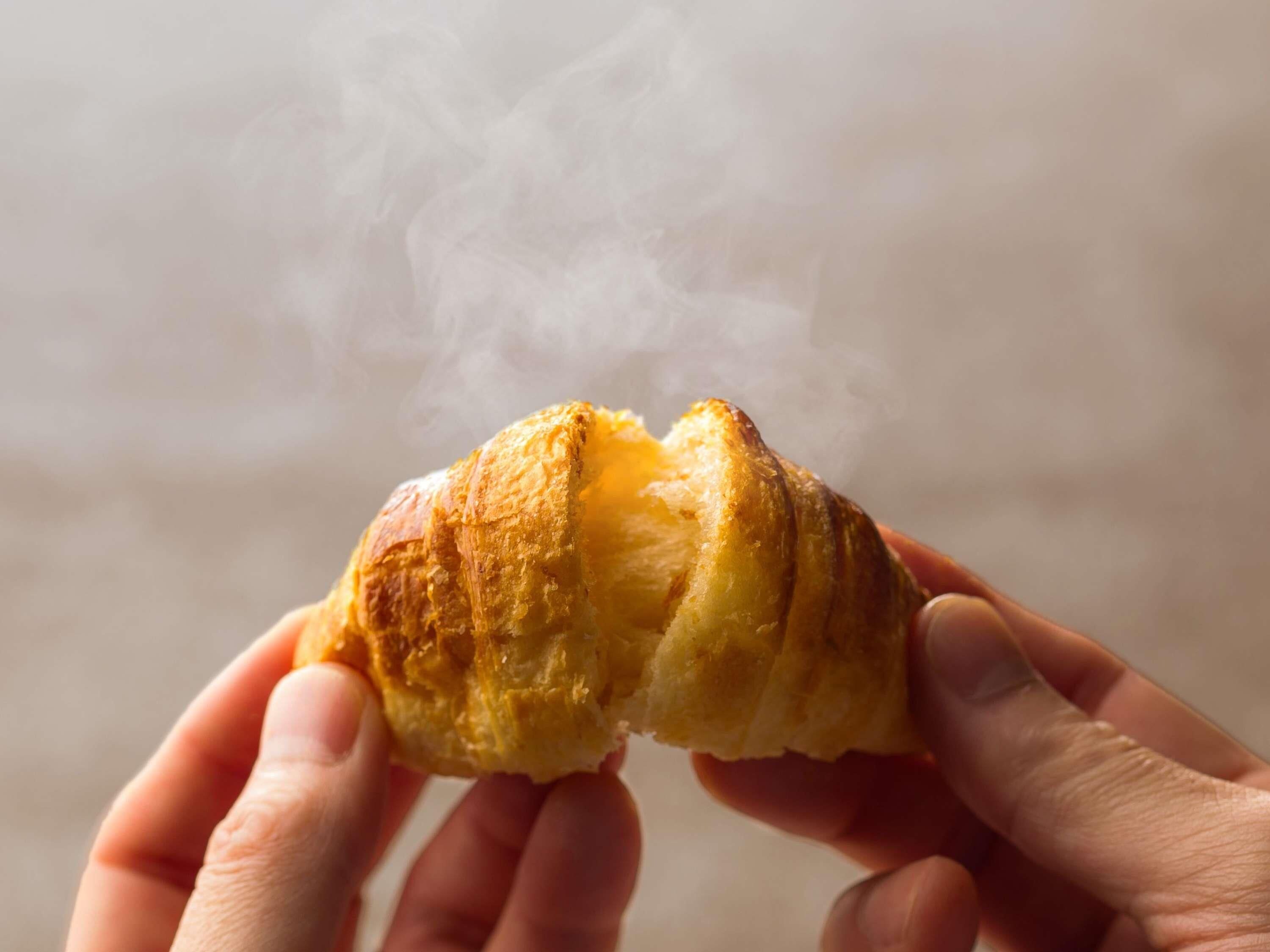 Uma mão segurando um croissant parcialmente comido, com vapor subindo.