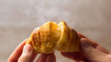 Uma mão segurando um croissant parcialmente comido, com vapor subindo.