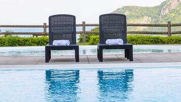 Duas cadeiras de vime com toalhas, uma piscina e uma cerca de madeira com vista para uma paisagem montanhosa.